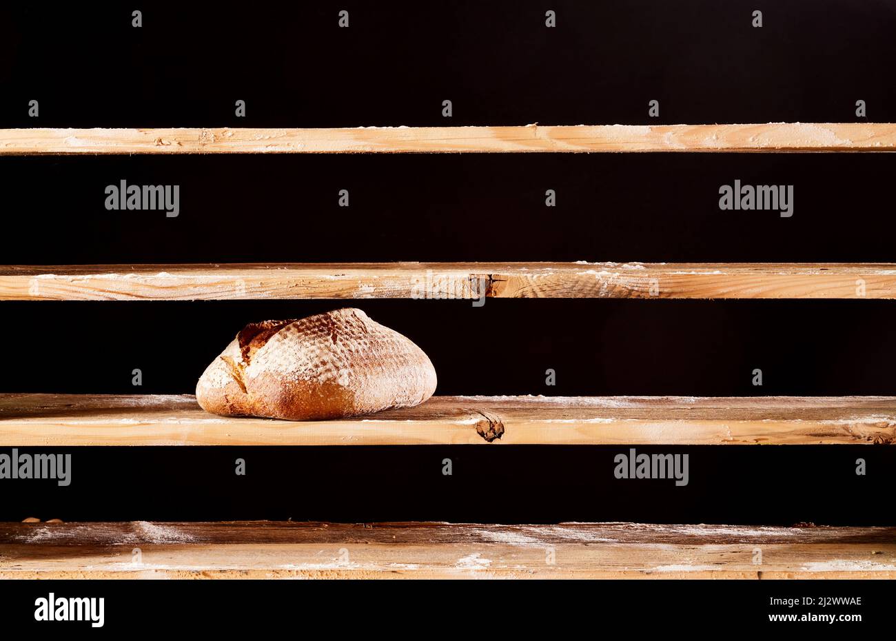 Loaf of baked bread with crust placed on empty wooden shelves in bakery ...