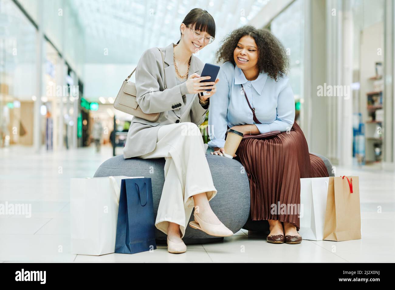 Full length portrait of two smiling young women using smartphone in ...