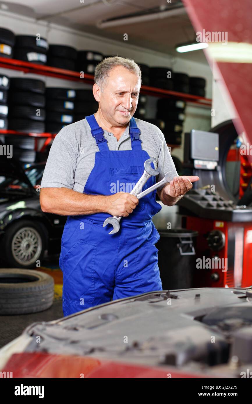 Pensive elderly cheerful positive smiling man mechanic looking at car ...