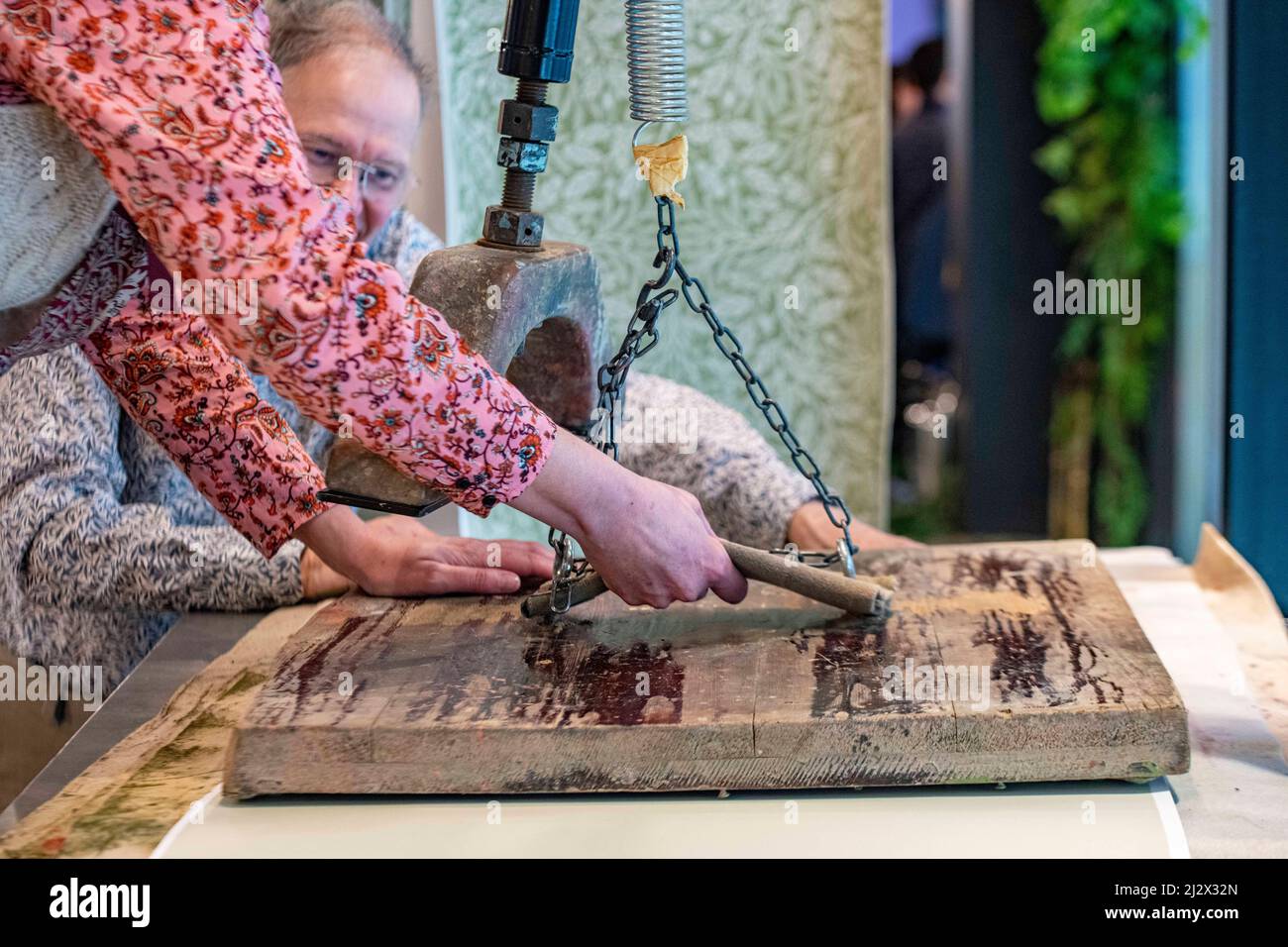 Hands press on a heavy block printer to create hand made wallpaper ...