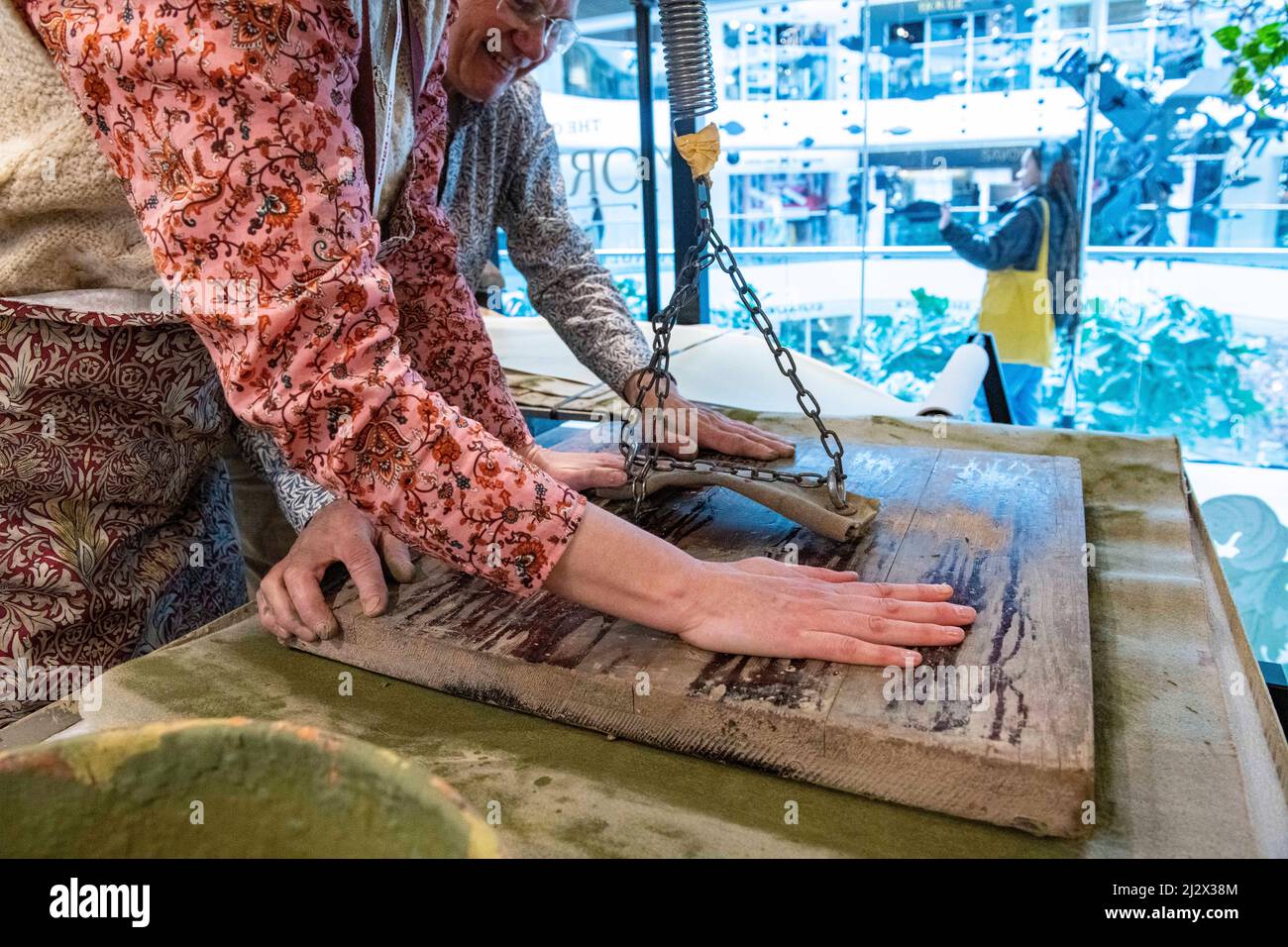Hands press on a heavy block printer to create hand made wallpaper ...