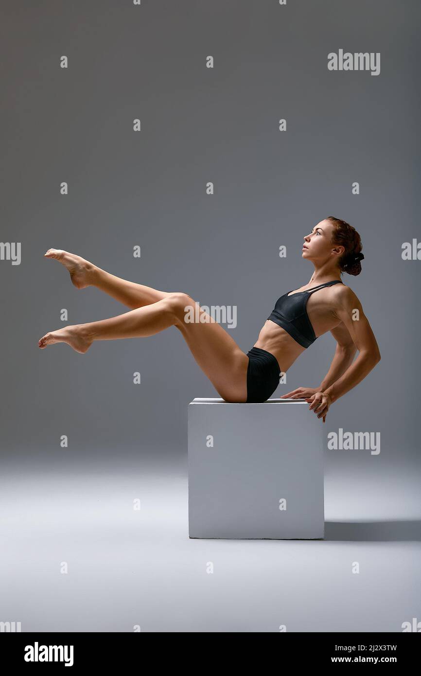 Flexible athletic woman in a sportswear doing splits in a fitness studio on a gray background ...