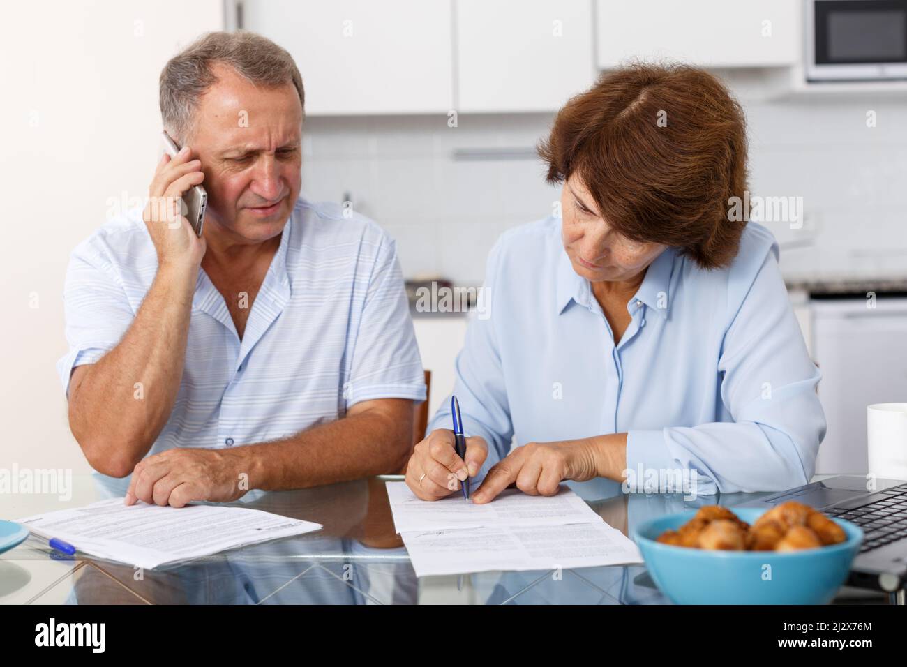 Mature family couple sitting at kitchen table with phone signing ...