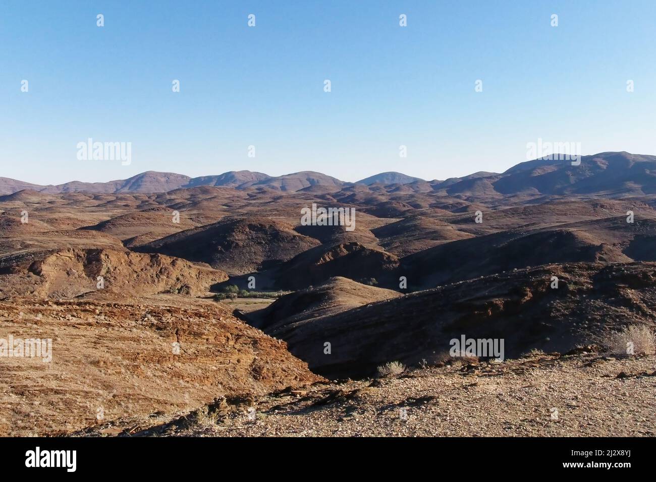 A desert in Namibia with hills and mountains against a clear cloudless ...