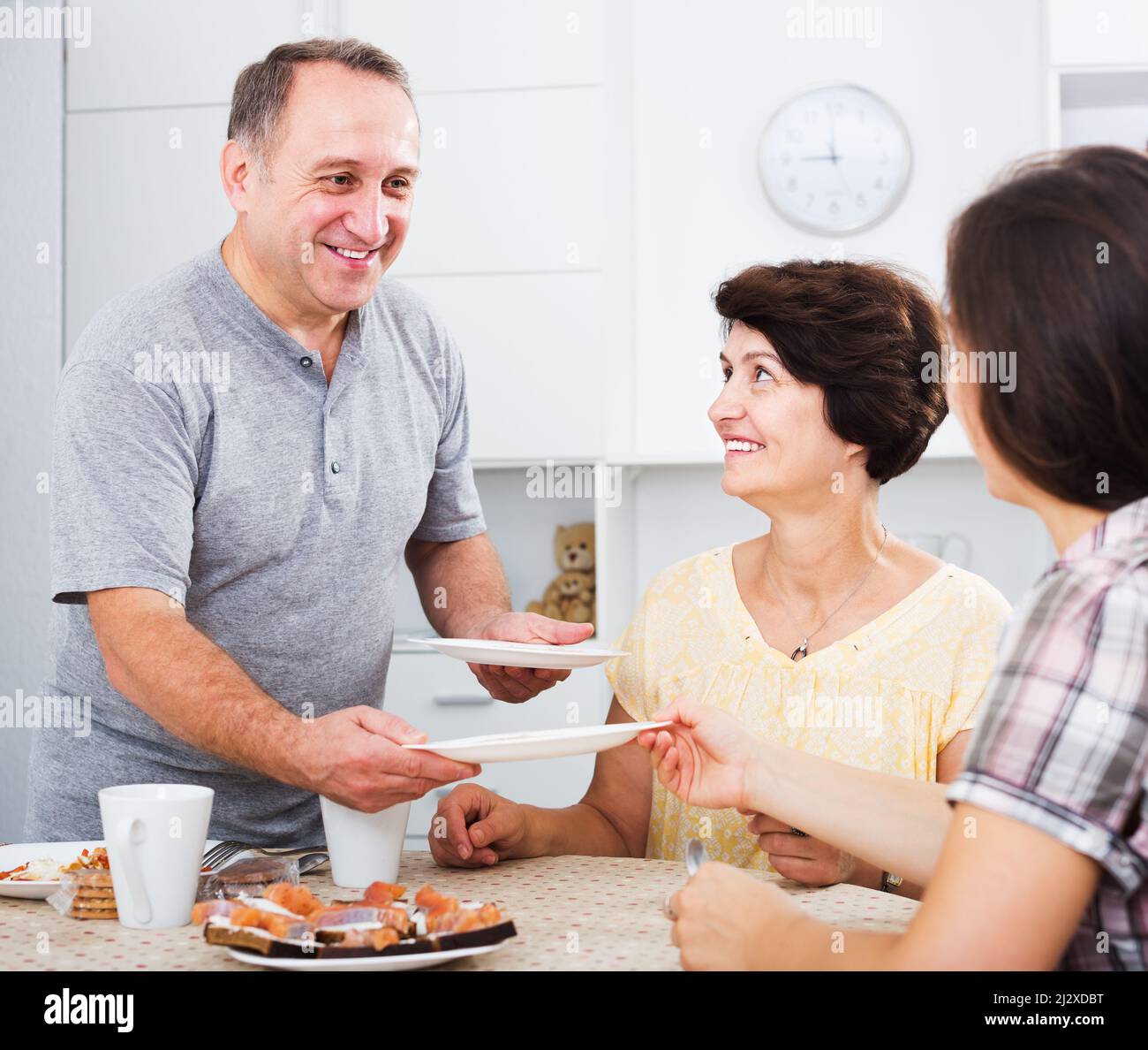 Glad mature man setting table for family lunch at home indoors. Focus ...