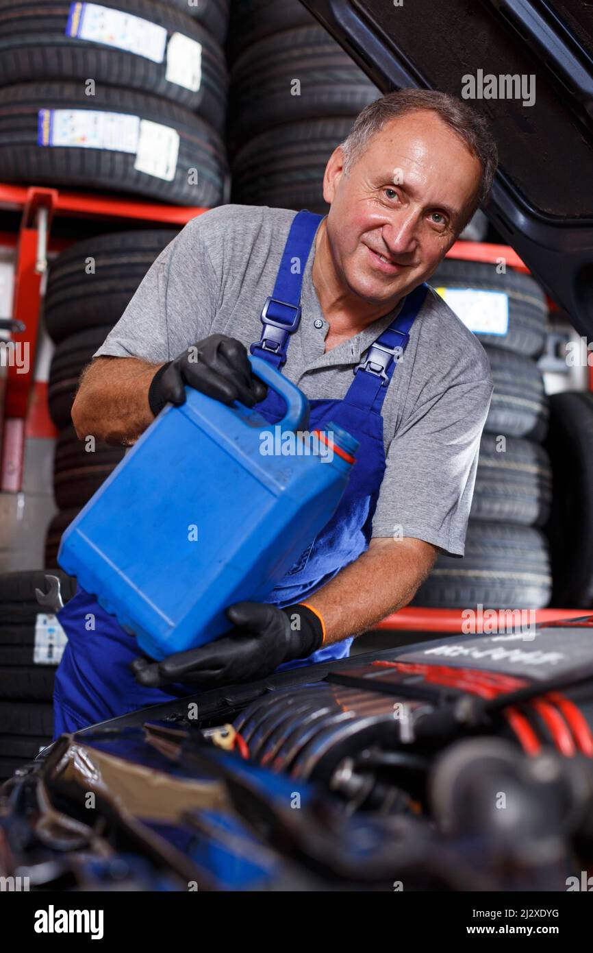 Skilled mature car mechanician changing motor oil in vehicle in auto ...