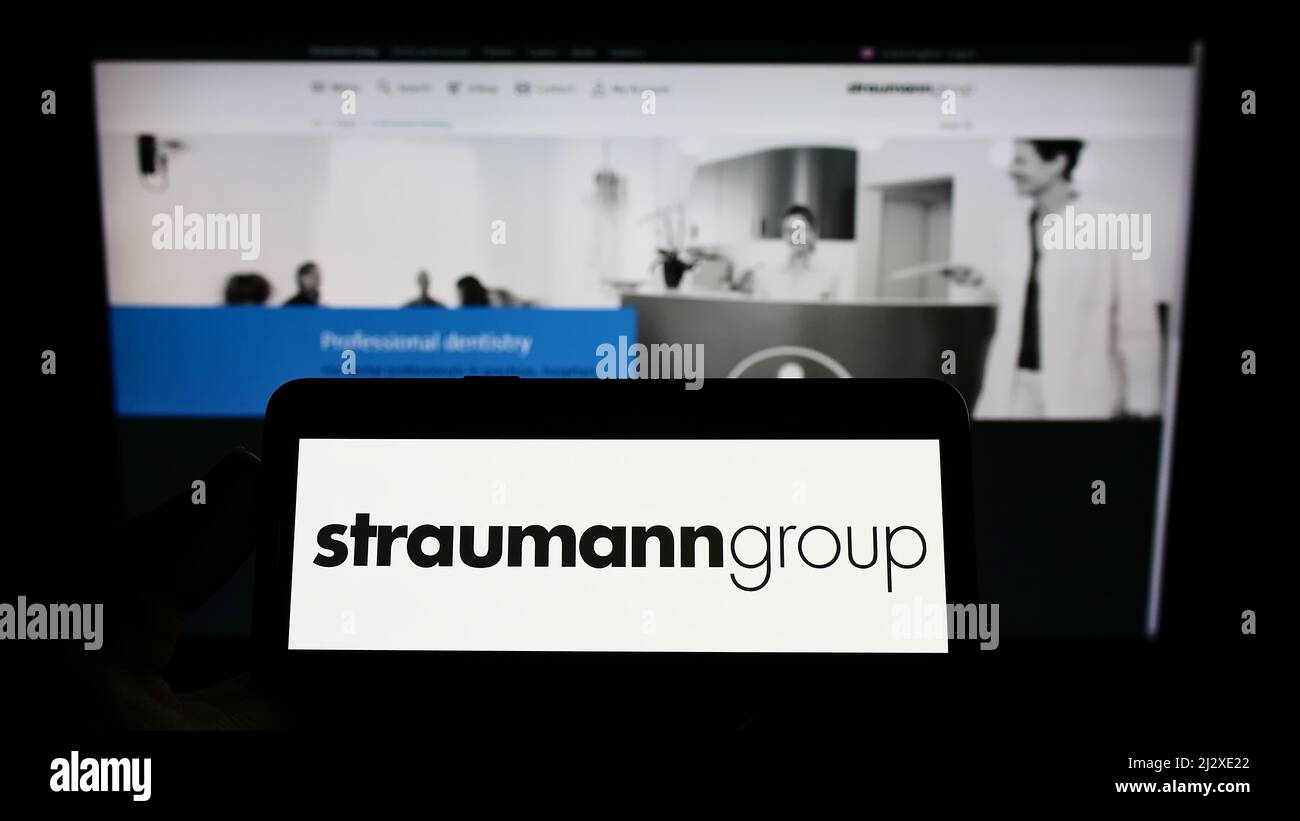 Person holding cellphone with logo of Swiss medical company Straumann ...