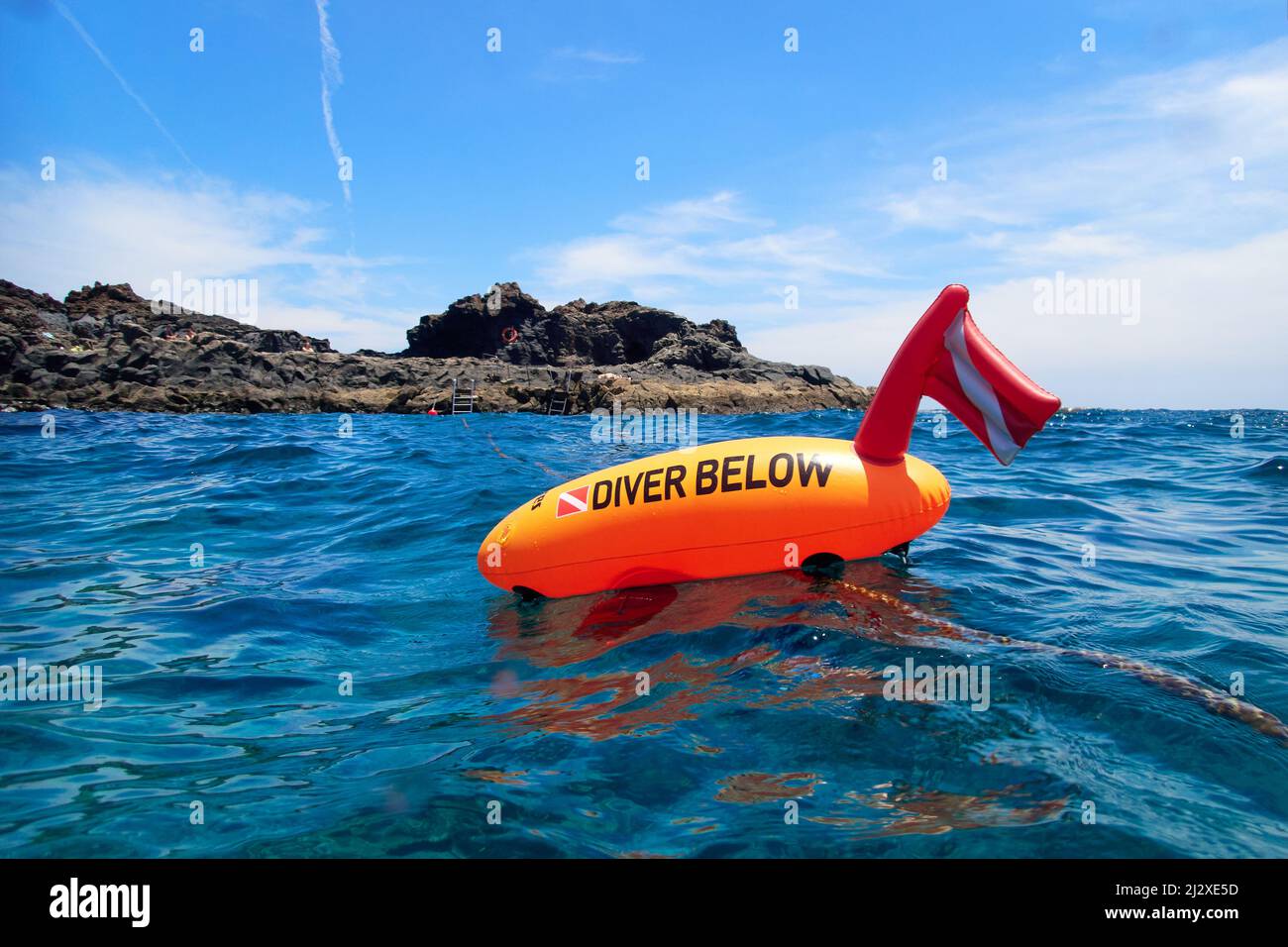 An orange diving buoy with text "Diver below" floats on the surface of ...
