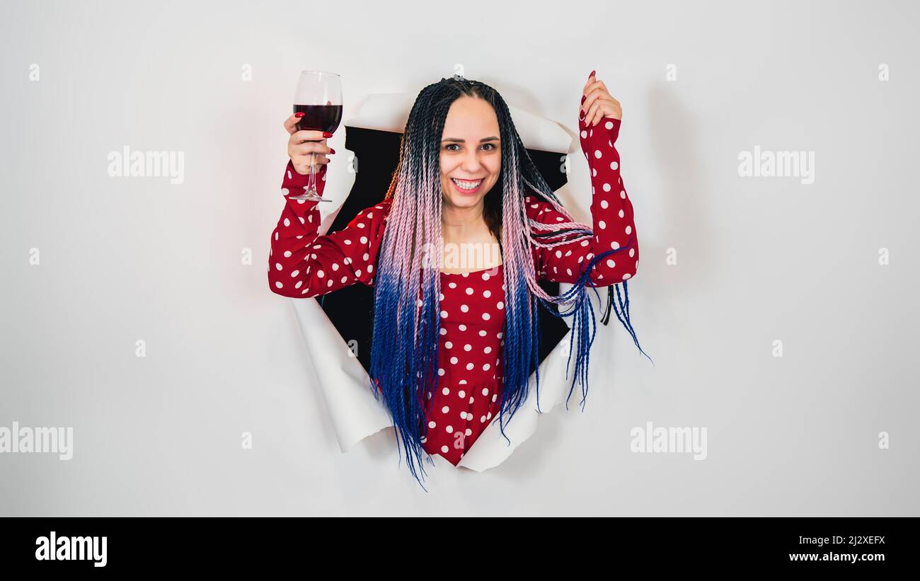 Young woman with glass of wine in studio. Beautiful female in red dress ...