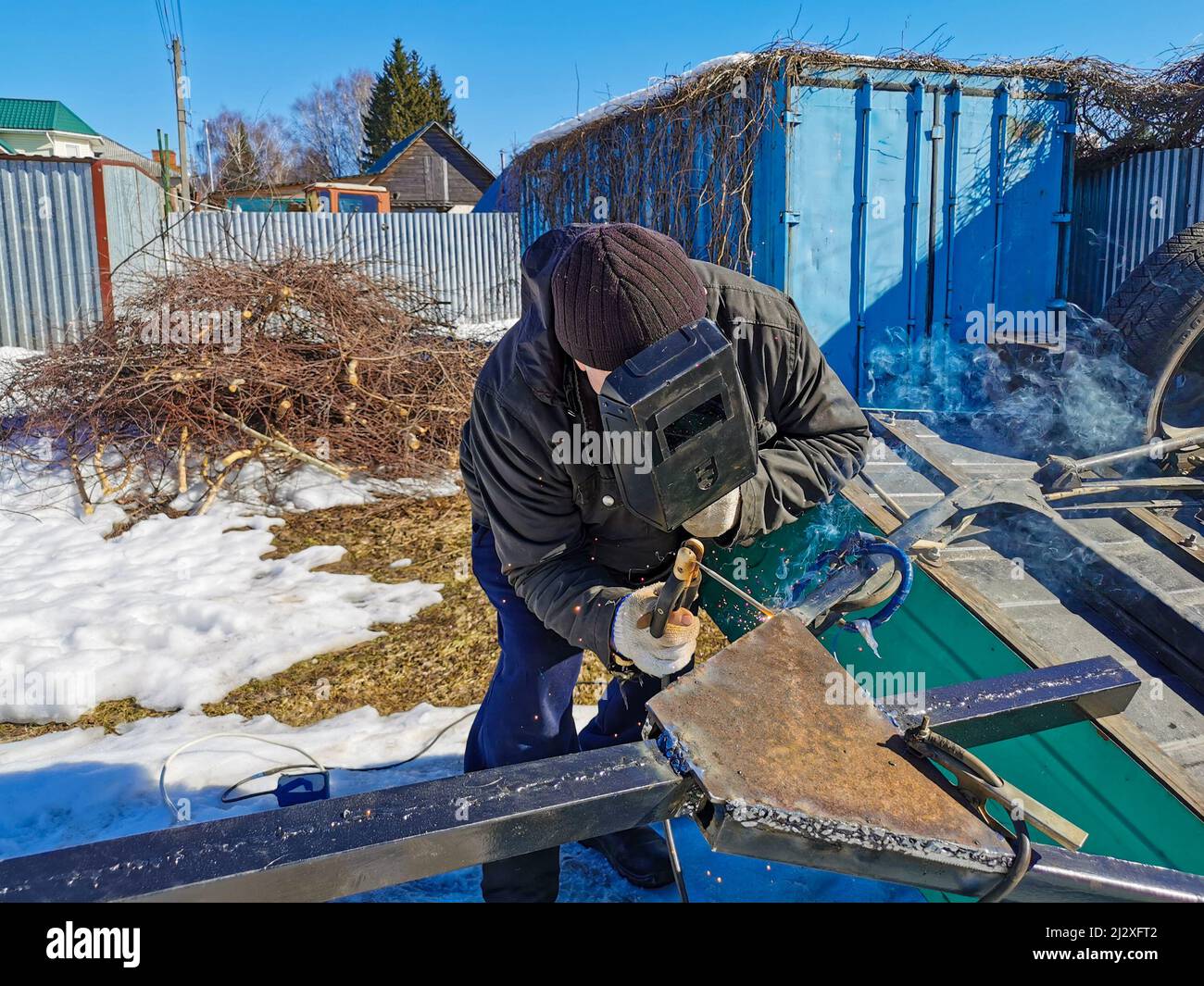 An elderly man foreman repairs a car trailer using electric arc welding ...