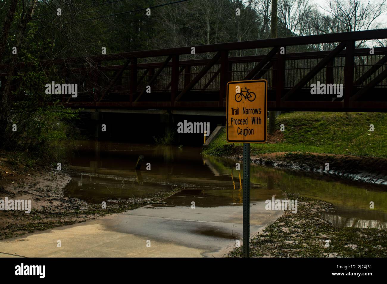 A trail sign next to the flooded trail going under the bridge in ...