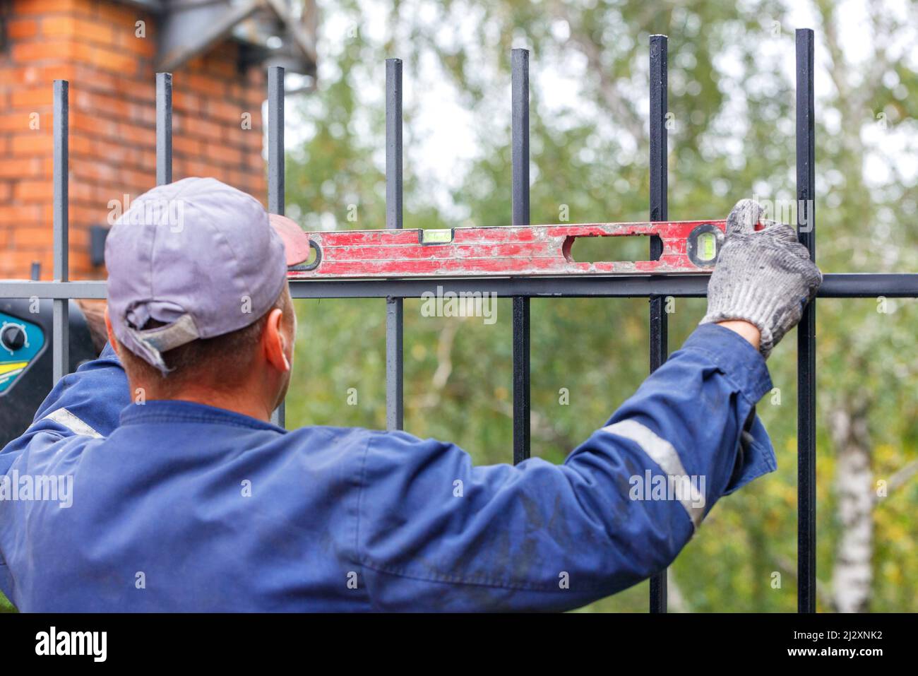 A builder is using an old level to level a metal fence while he is ...