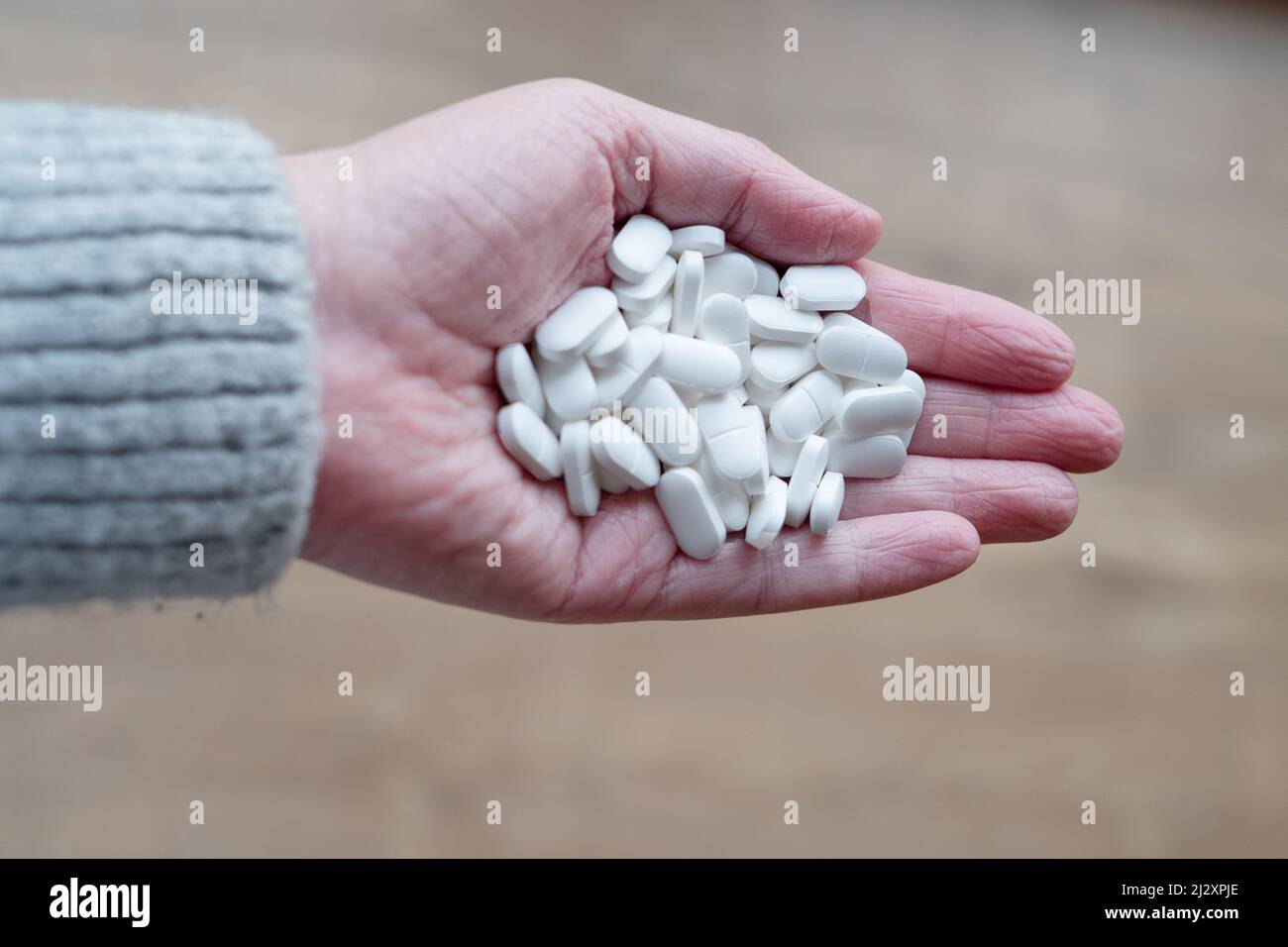 A middle aged woman holding a large handful of white paracetamol ...