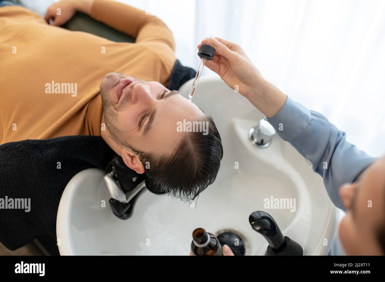 Beautician applying hair serum on mans head Stock Photo - Alamy