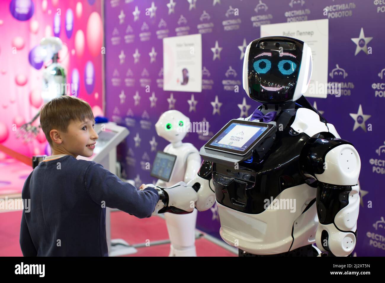 The boy is talking, playing with an android robot at the exhibition ...