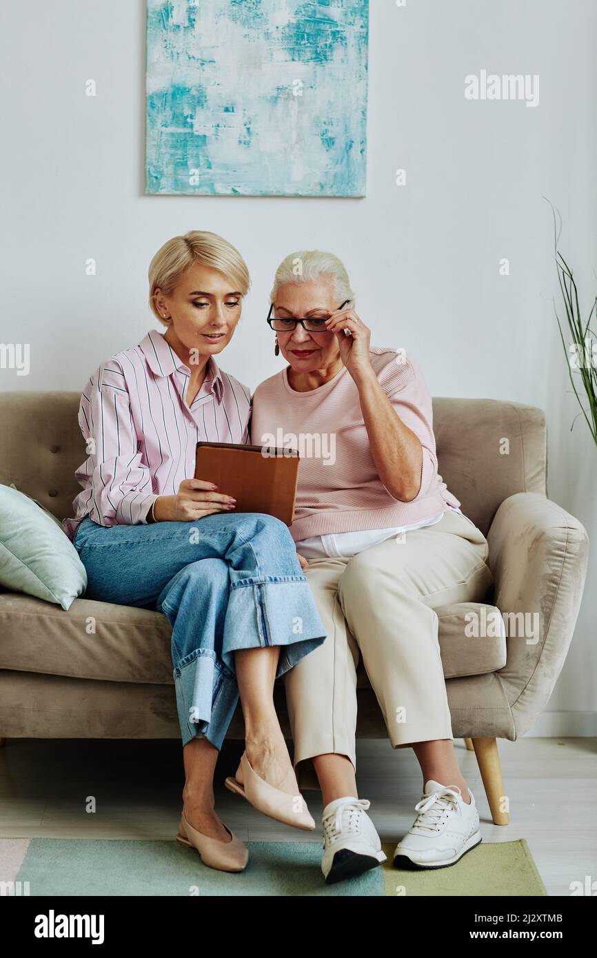 Vertical portrait of young woman helping senior mother using digital ...