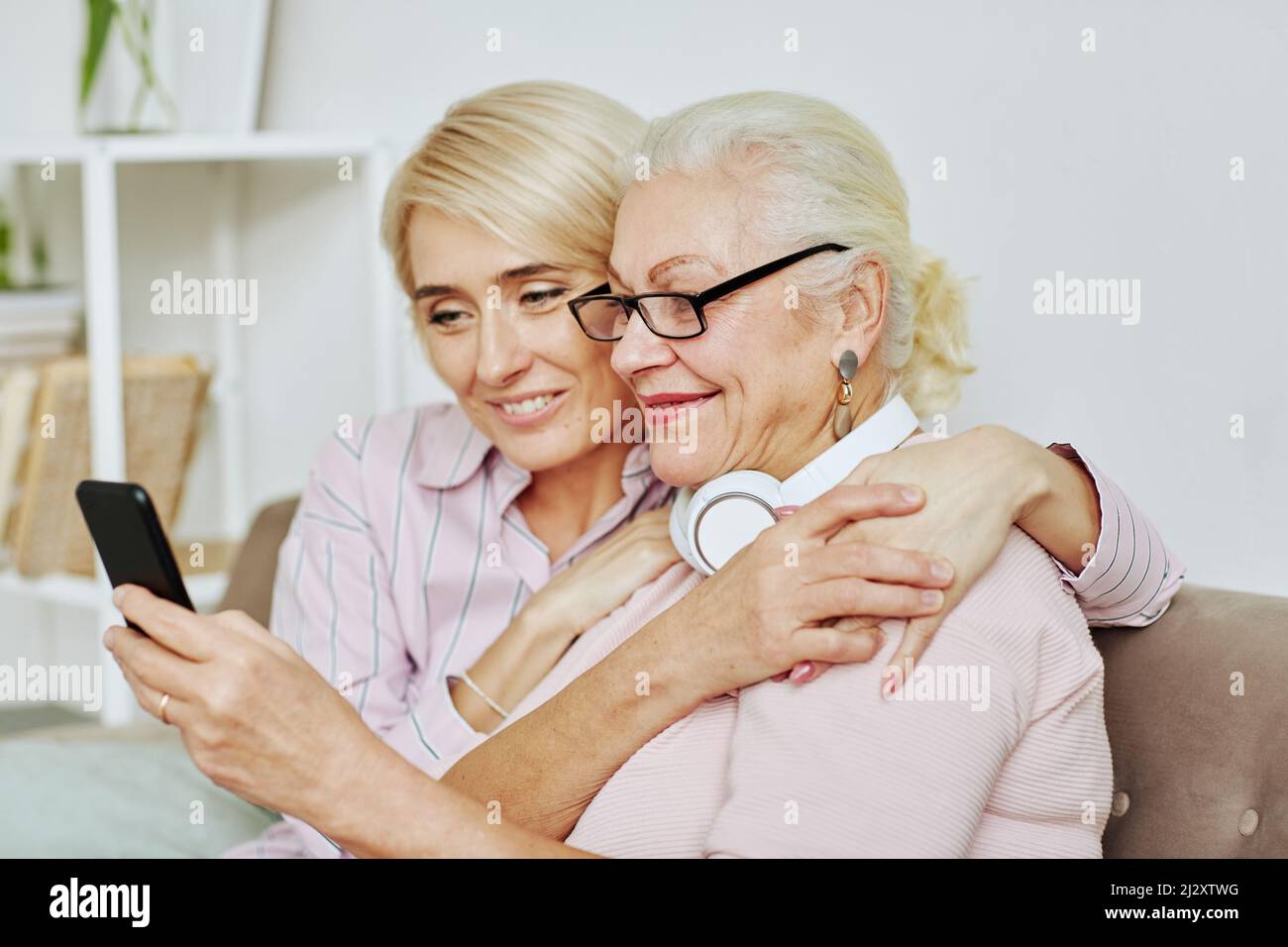 Portrait of smiling adult daughter embracing senior mother and looking ...