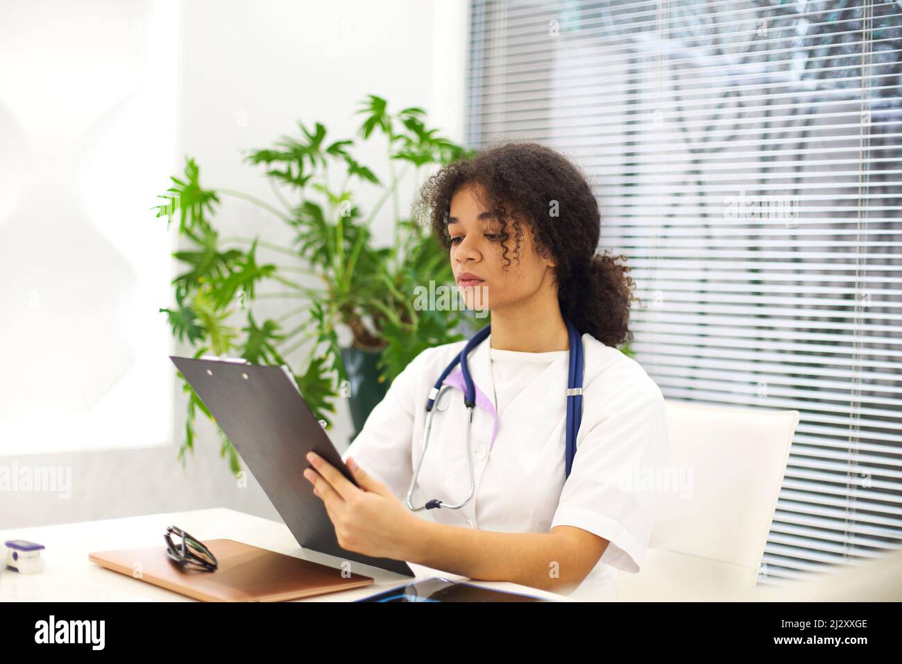 Ethnic female medic in mask and uniform filling medical report on ...