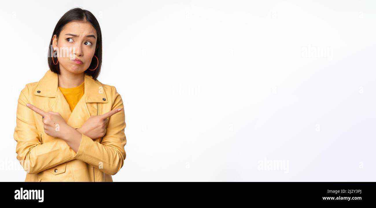Image of indecisive asian girl, pointing fingers sideways, pointing ...