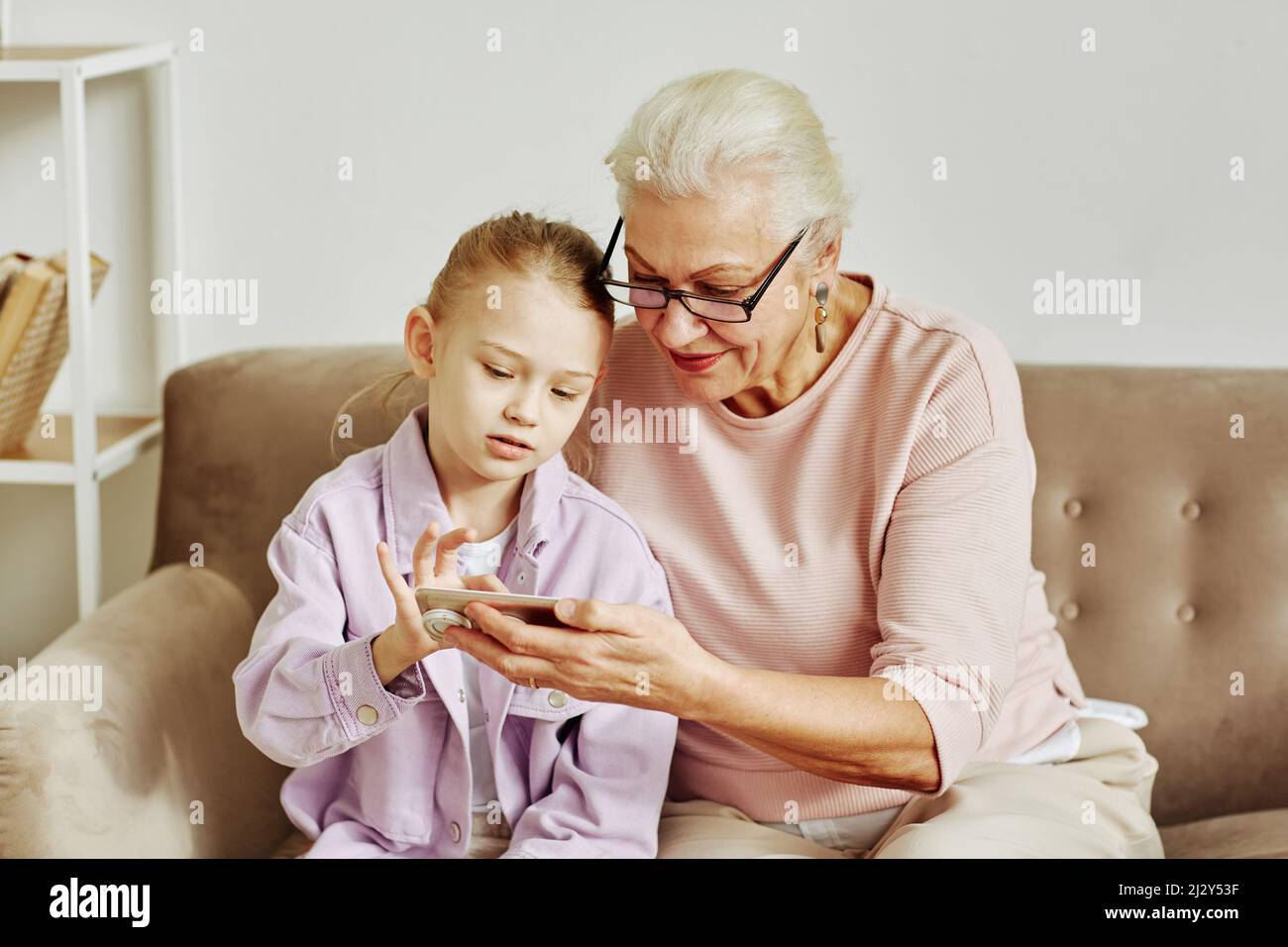Portrait of young girl showing smartphone to grandmother and teaching ...