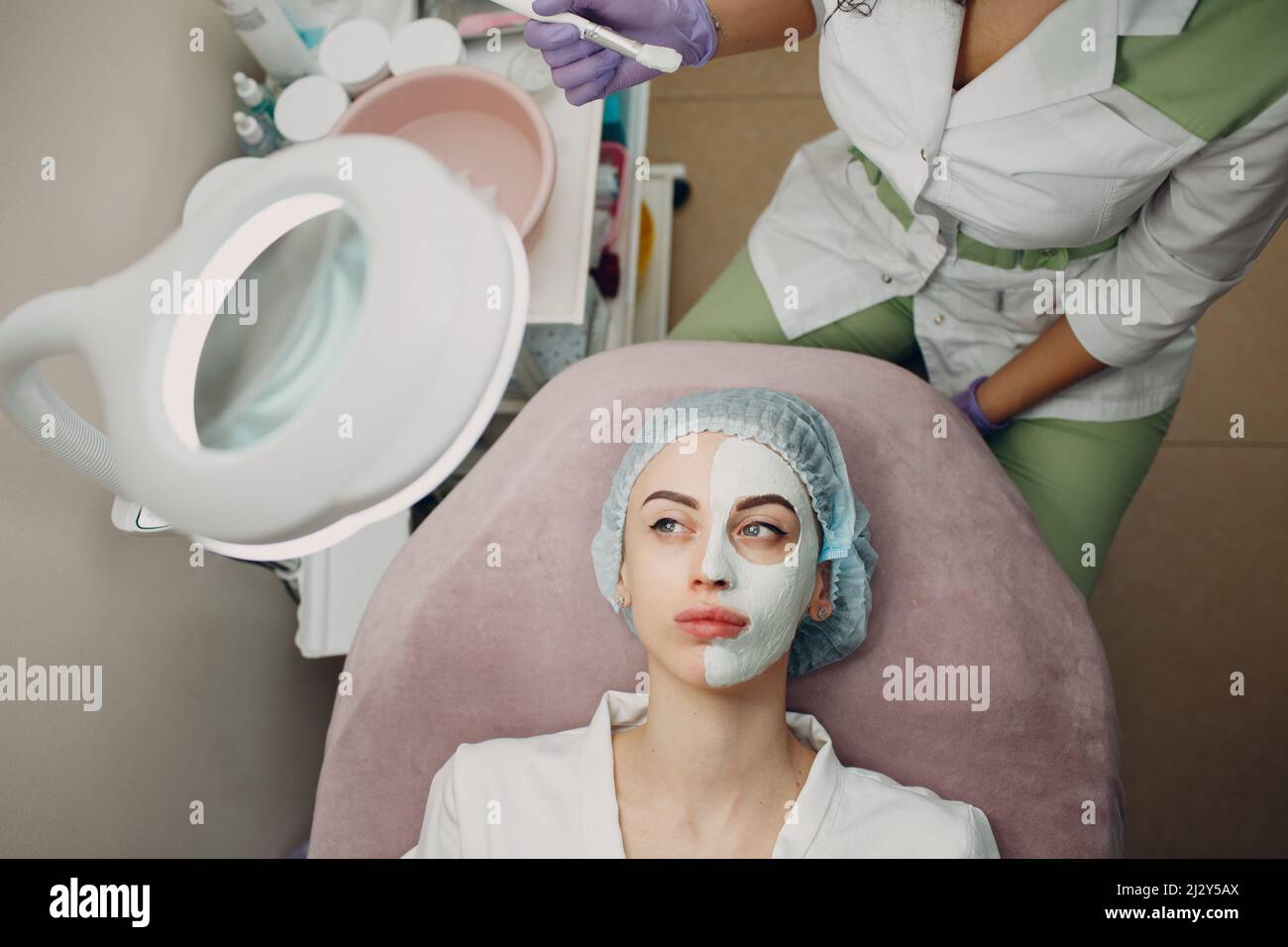 Young woman applying mask of clay on face in overhead top view beauty ...