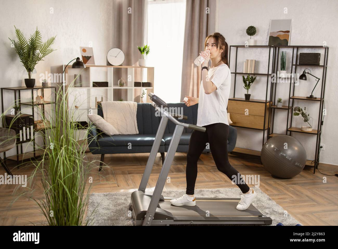 Fit athletic woman running on the treadmill while drinking water from a ...