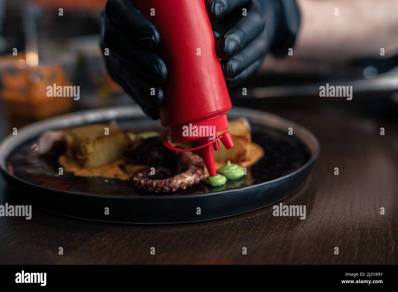 Chef preparing octopus with potatoes on pea mash decorated with edible ...