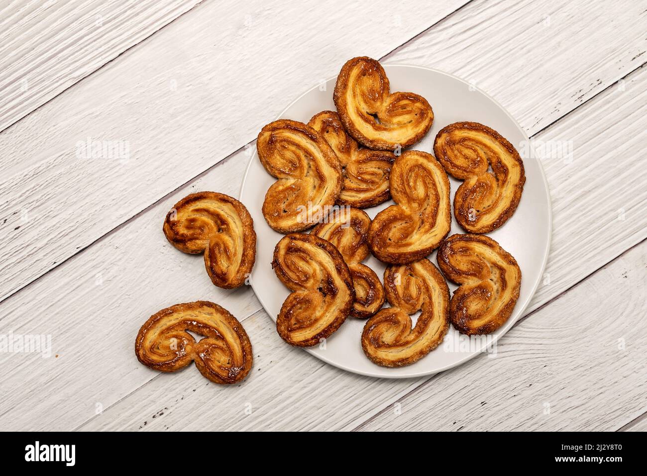 Palmier puff pastry biscuits in white plate on a white painted wooden ...