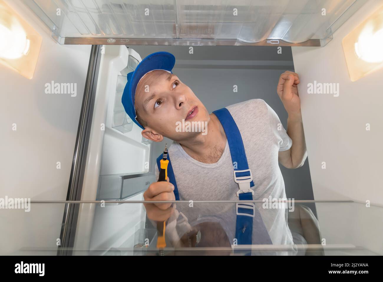 Male technician in overalls repairs a broken refrigerator with a ...
