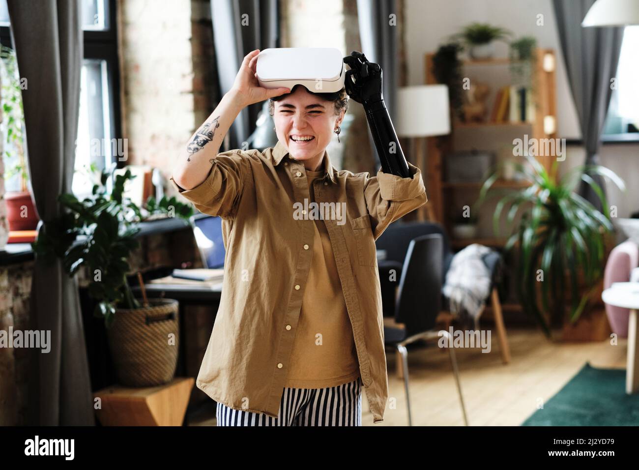 Happy woman with prosthetic arm taking goggles off after virtual game ...