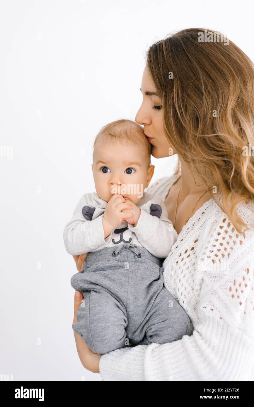 A young mother holds her little son in her arms and kisses him on a white background Stock Photo ...