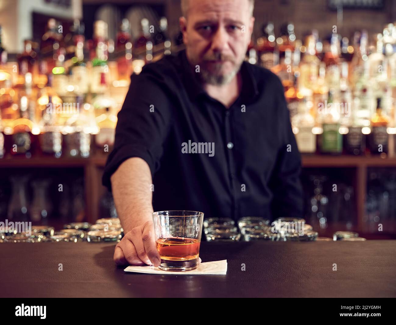 Male bartender serves a glass of neat whiskey on the bar counter at the ...