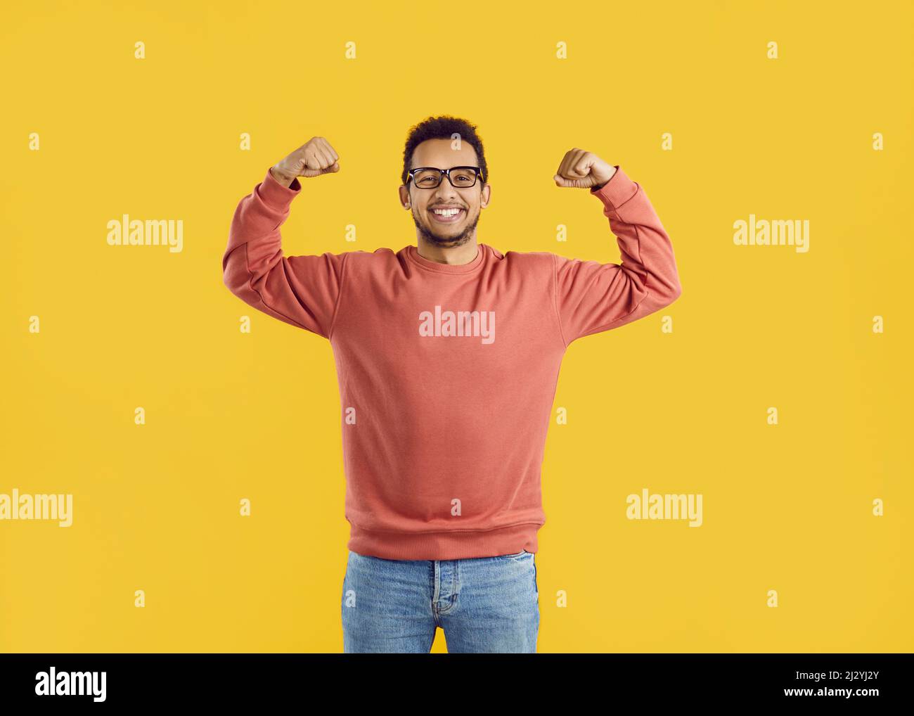 Happy funny young man in sweatshirt and glasses flexing his arms to ...