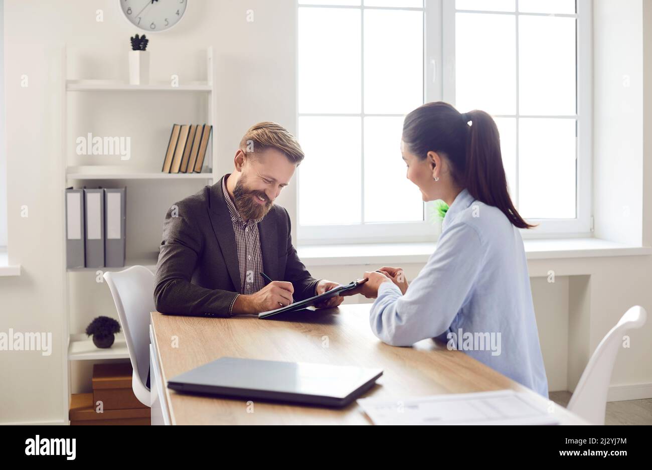 Happy man sitting at desk with bank worker and putting his signature on ...