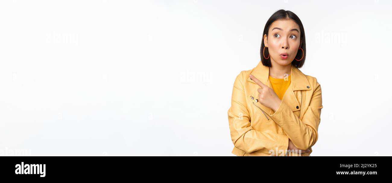 Image of surprised aisan woman pointing finger left, looking at logo or ...