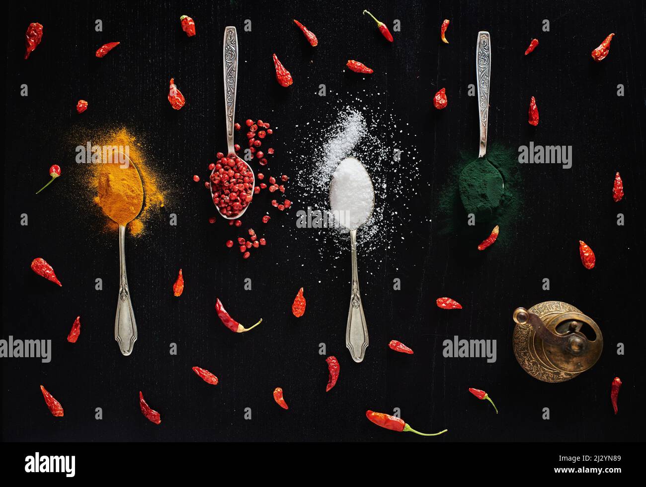 Various types of spices displayed on black background in tea spoons ...