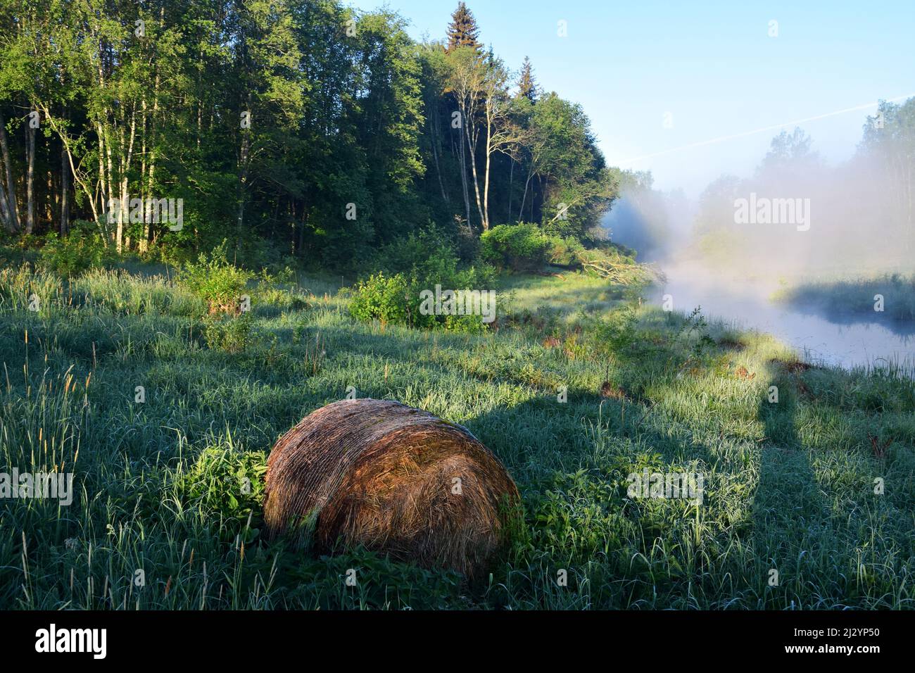 A haystack on the grass at a beautiful lakeside with a layer of mist ...