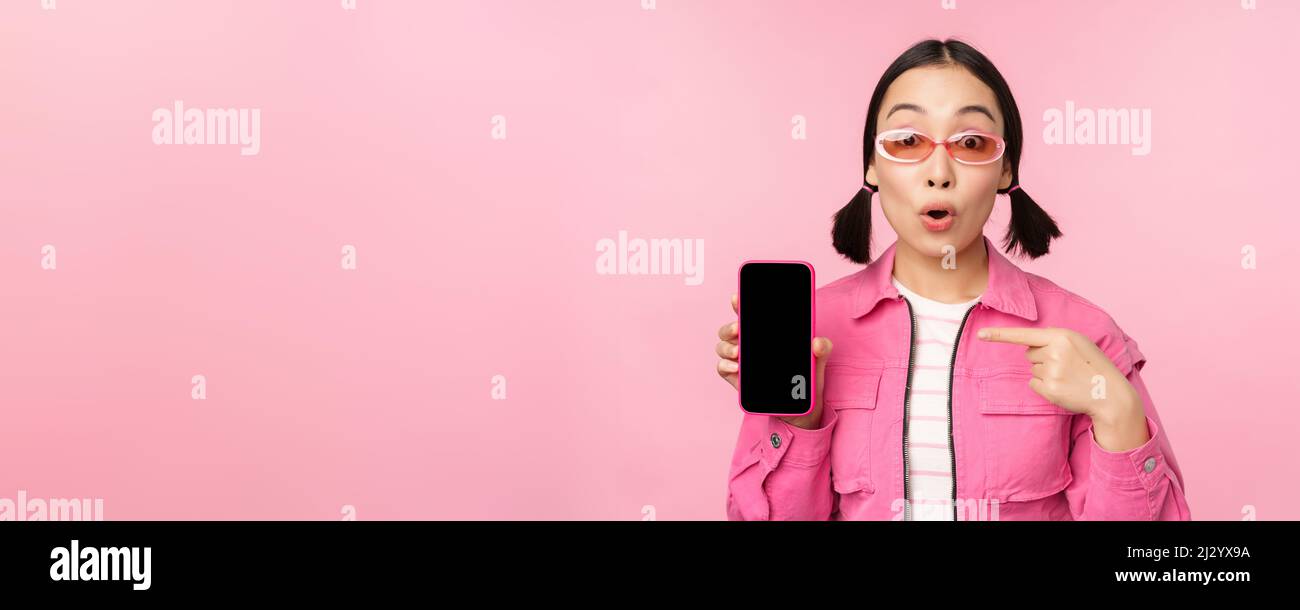 Enthusiastic asian woman in stylish clothes, sunglasses, pointing ...