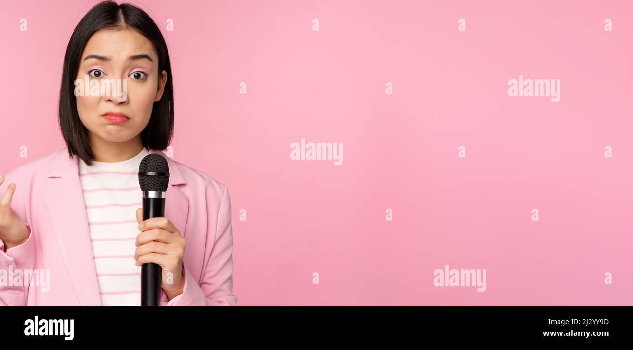 Indecisive, nervous asian business woman holding mic, shrugging and ...