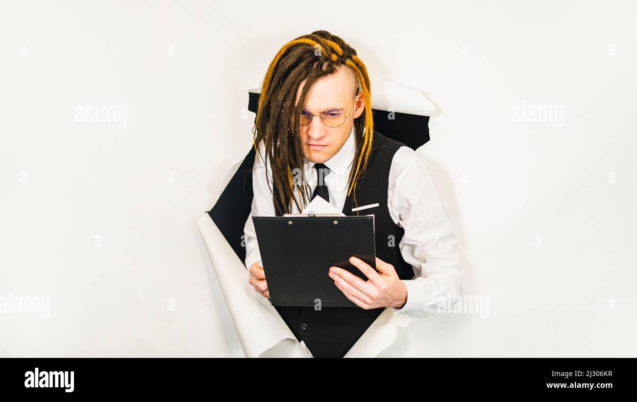 Young man in glasses with dreadlocks looks at clipboard. Handsome male ...