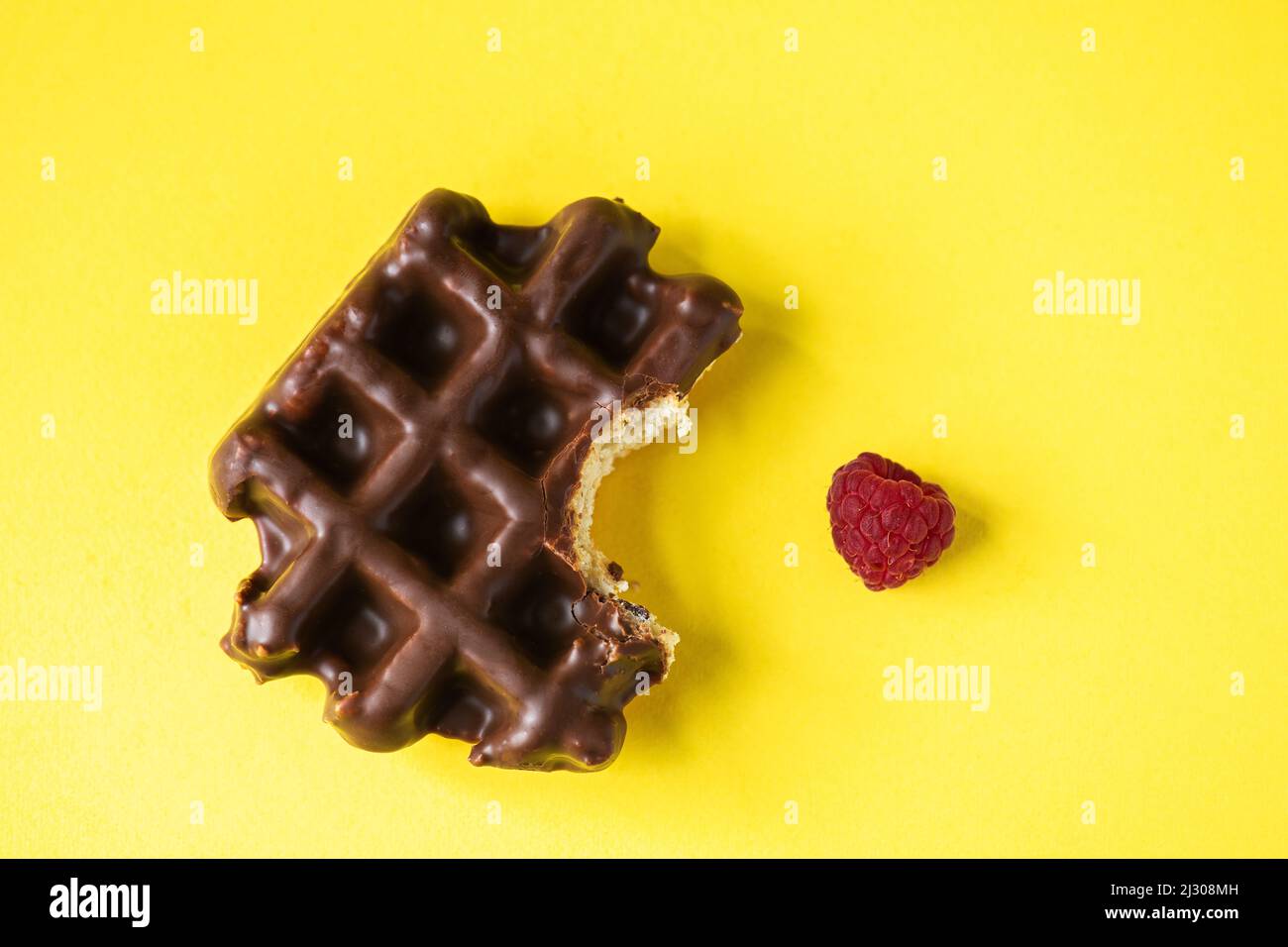 Bitten off chocolate waffle and raspberry, yellow background, top view ...