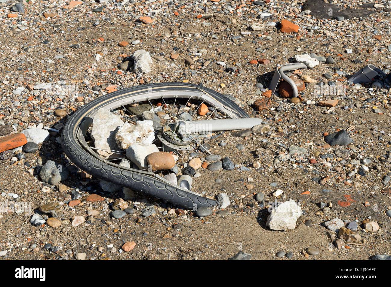 The wheel of a bicycle washed up and buried on the stony beach ...