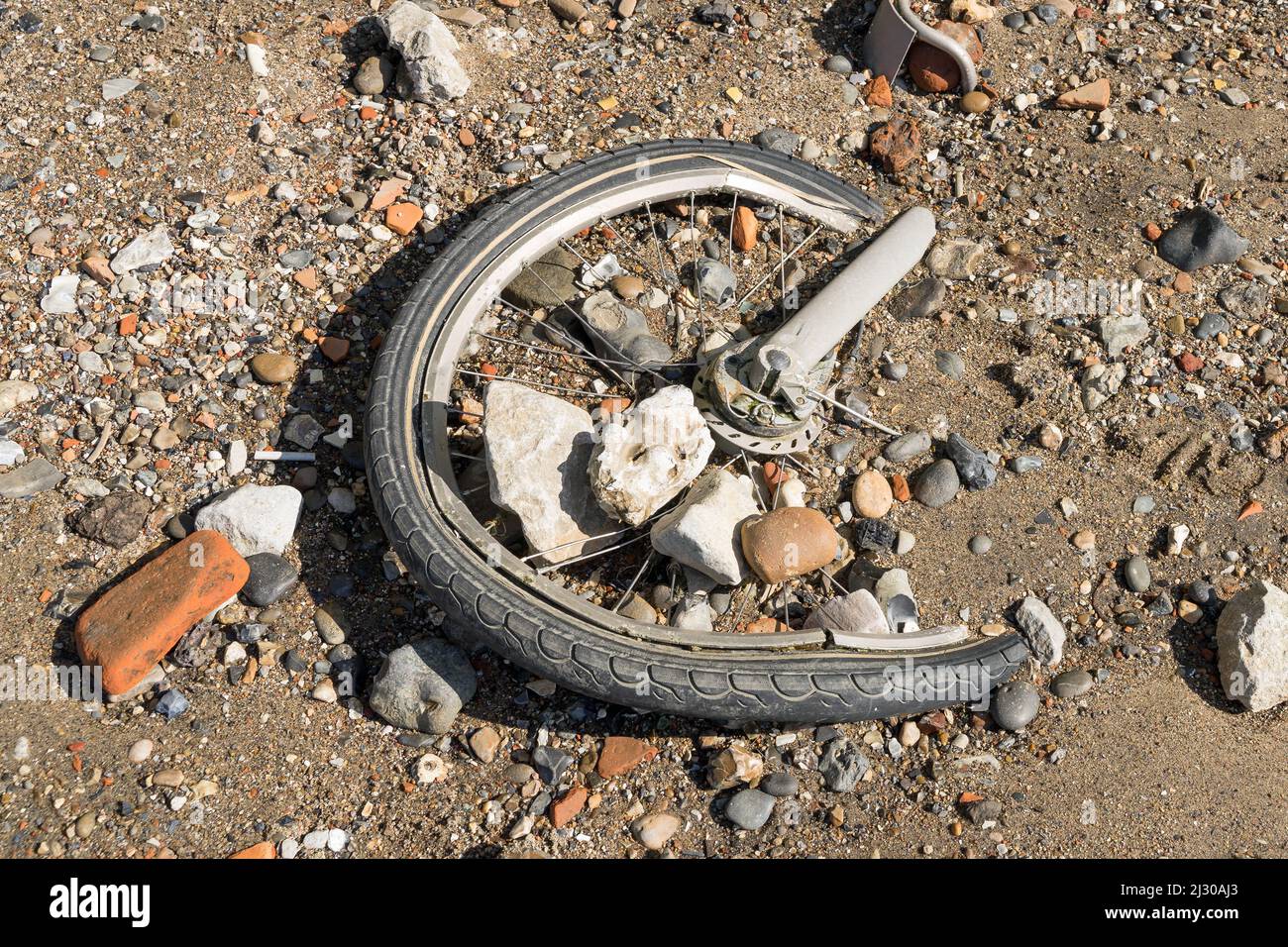 The wheel of a bicycle washed up and buried on the stony beach ...