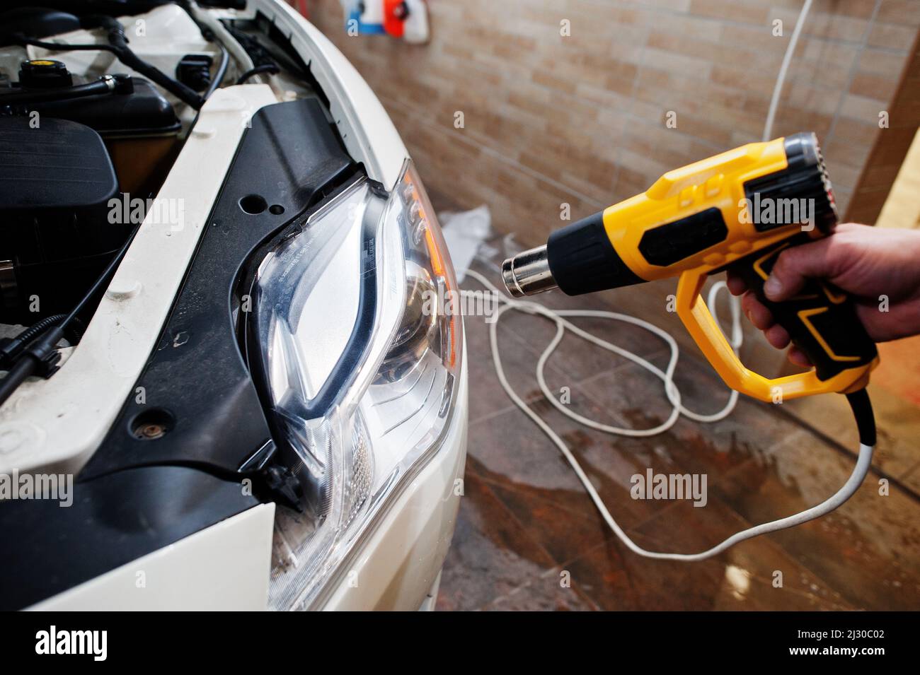 Worker in detailing garage hold hot air blower in white luxury car ...