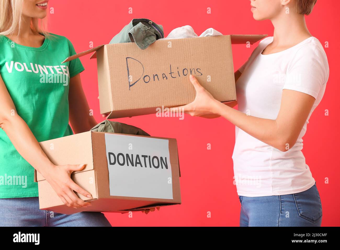Young women holding boxes with clothes for donation on red background ...