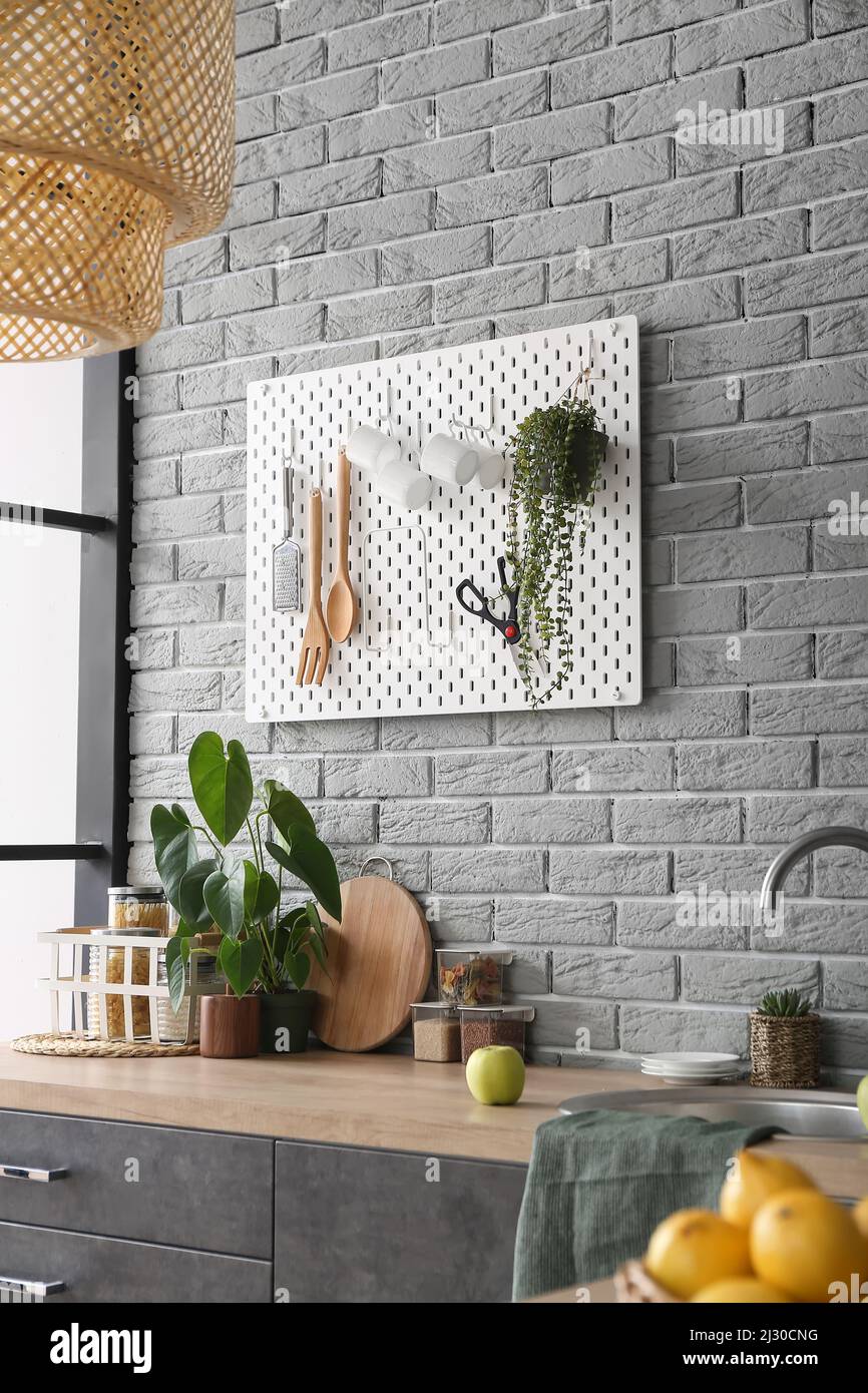 Pegboard with kitchenware on grey brick wall in modern kitchen Stock ...