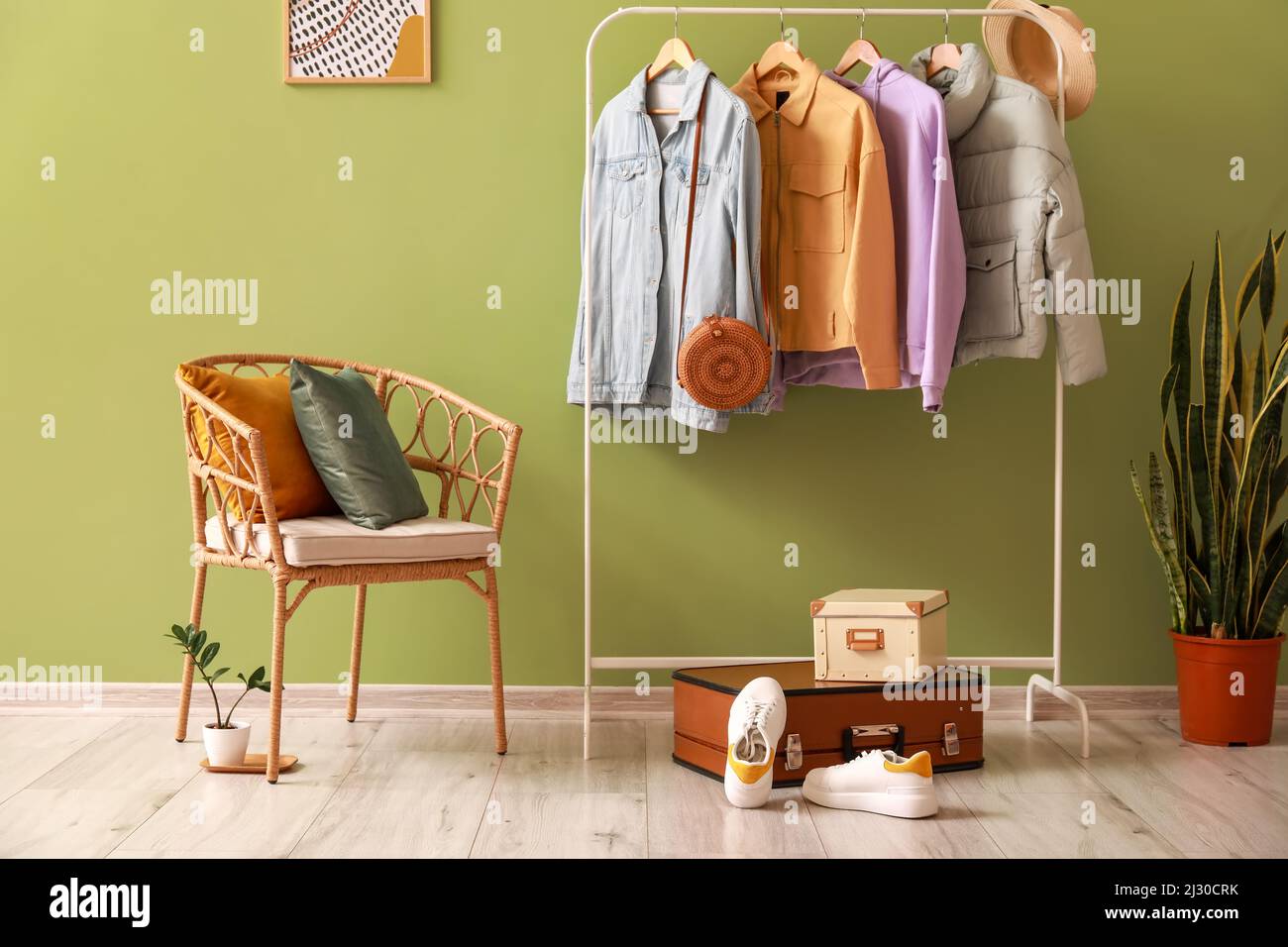 Rack with stylish jackets and chair near color wall in room interior ...