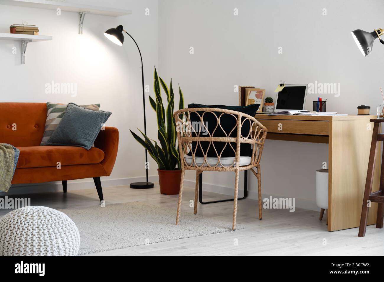 Modern workplace with laptop, wicker chair and red sofa in living room ...