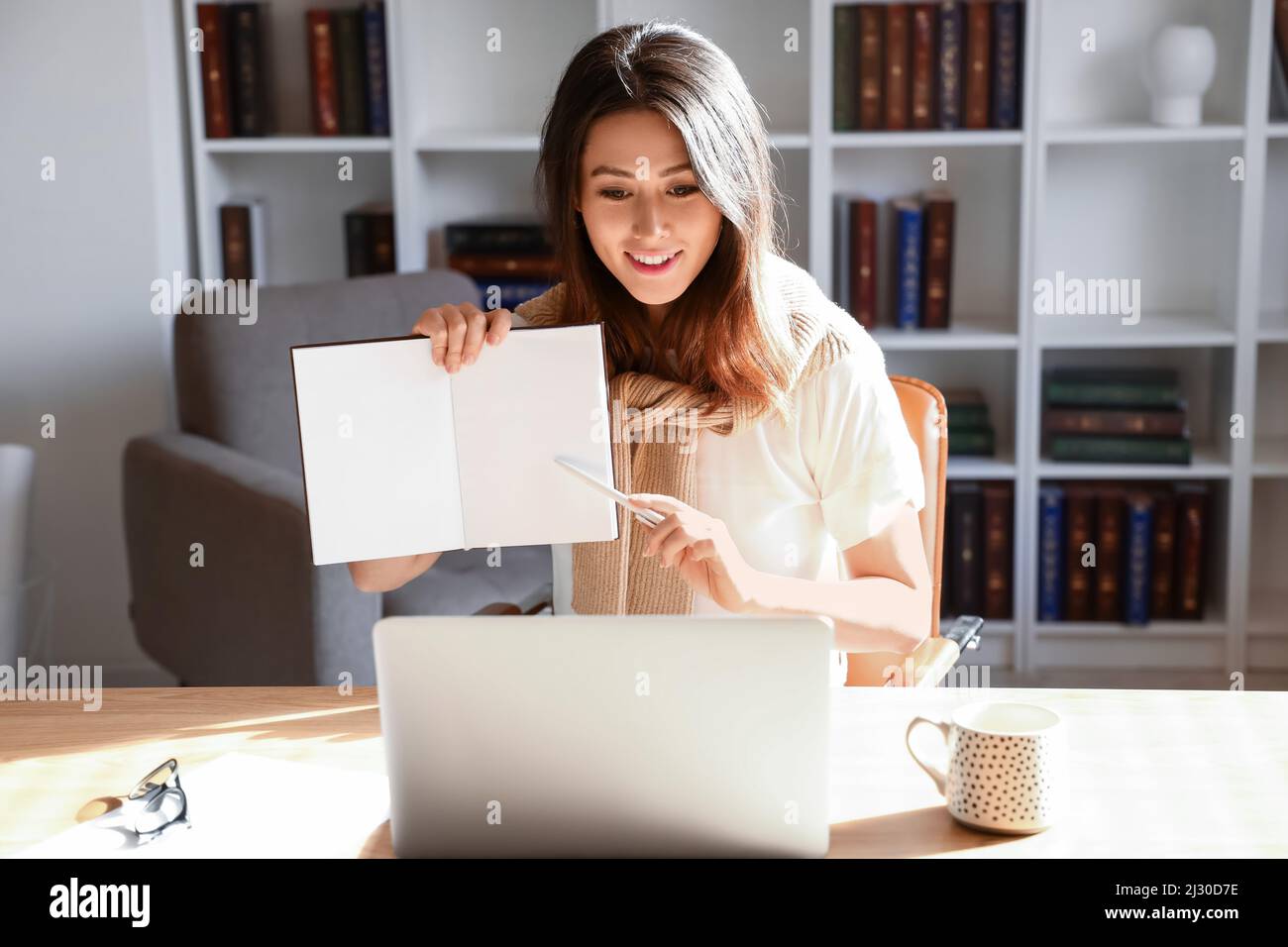 Young Asian tutor with book giving lesson online at home Stock Photo ...