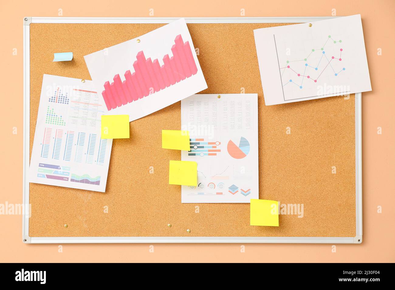 Board with blank sticky notes and charts hanging on beige wall Stock ...